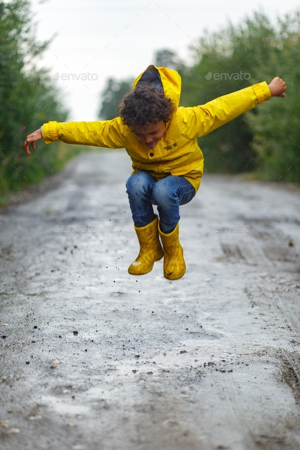 Kid playing in the rain in autumn park. Child jumping in muddy puddle ...