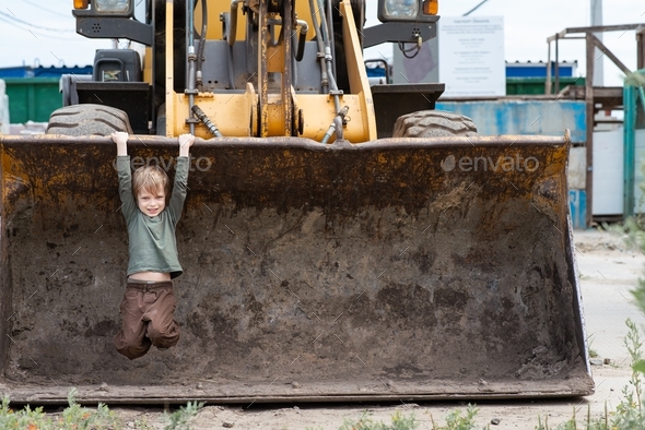 smiling boy hanging on big backhoe loader and looks into the camera ...