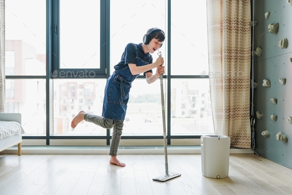 Teenage boy singing into the mop, listening to music in wireless ...