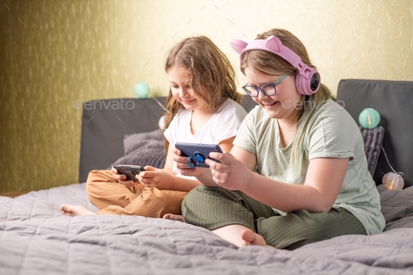 two teenage girls play online games on gadgets, at home on the bed, generation Z Stock Photo by ...