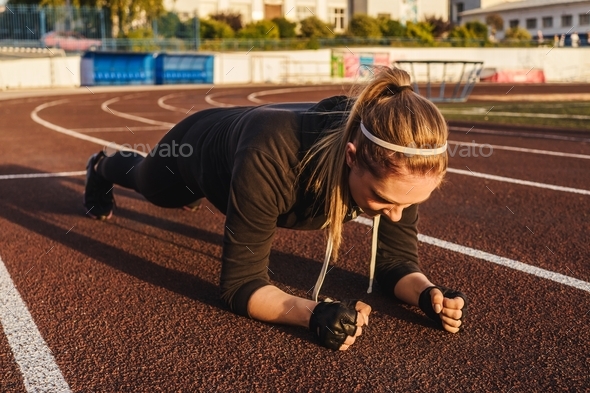 Young athletic woman doing plank exercise on running track. Sunset ...