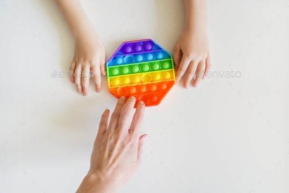 Pop it fidget in kid's hands with man's hand. Colorful toy push pop it ...