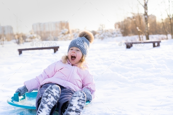 little girl rides down the slide on the ice, cheerful child, emotions ...