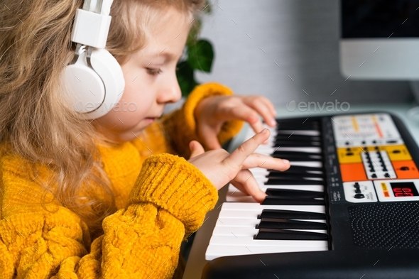 A little blonde girl in white headphones plays a synthesizer, child ...
