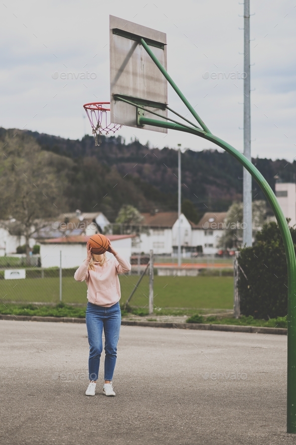 A woman plays basketball and trying to throw a ball through the hoop on ...