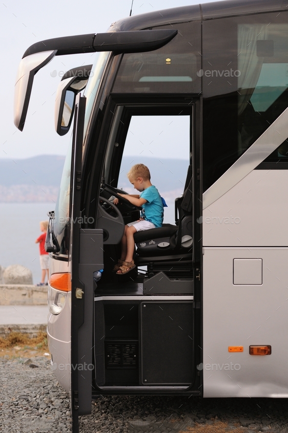 Little child sitting in the bus on the drivers sit and steering the ...