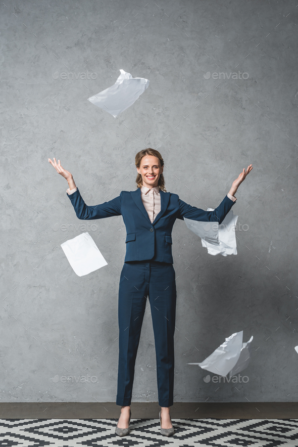 smiling businesswoman in suit looking at camera while throwing ...