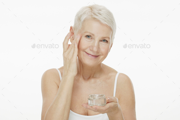 Senior woman applying moisturizing face cream, isolated on white ...
