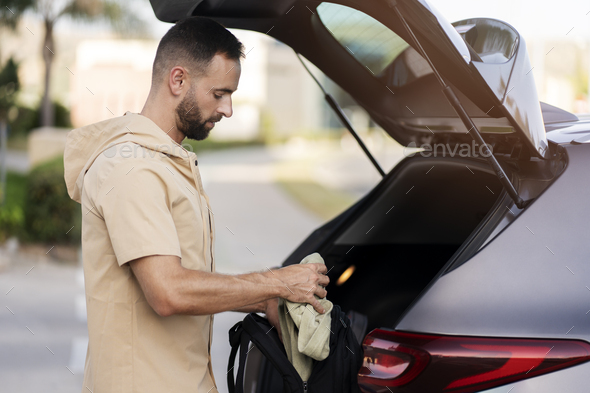Latin man loading bag in car trunk. Driver planning road trip ...