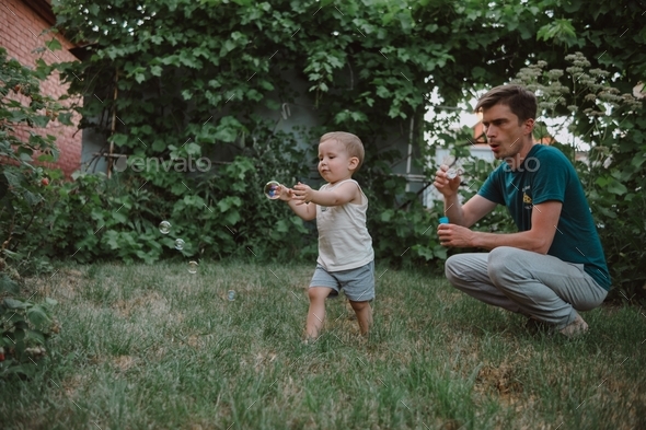 dad and baby launch soap bubbles in the backyard garden of the house ...