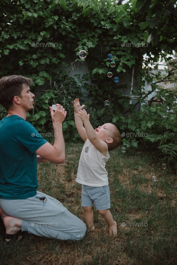 dad and baby launch soap bubbles in the backyard garden of the house ...