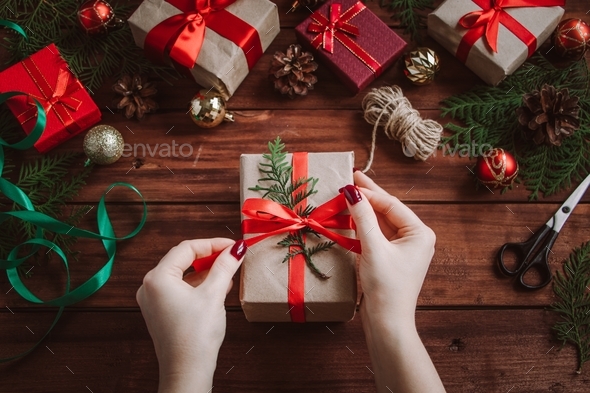 Christmas gift wrapping process. Woman decorates box with a red ribbon ...