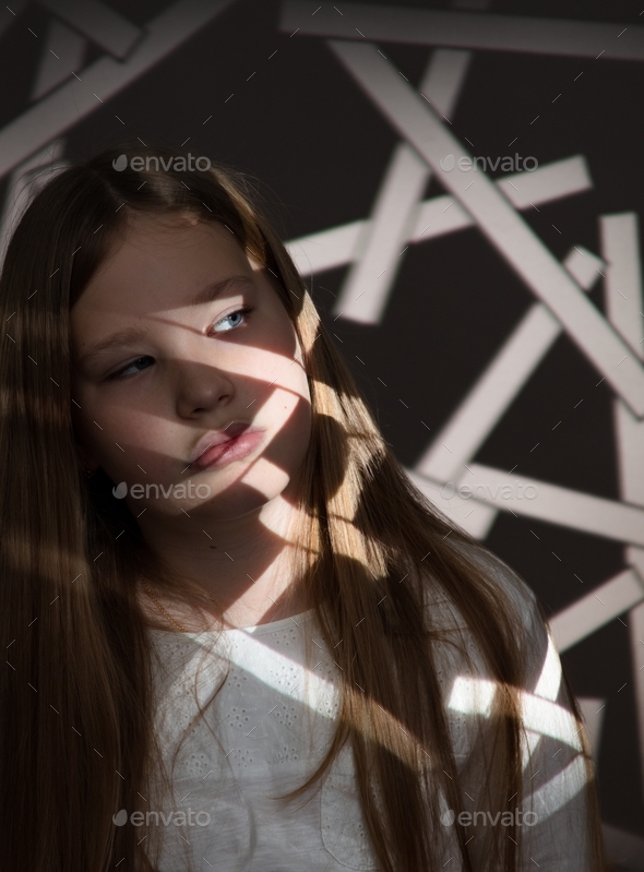 Close-up of thoughtful girl looking away against window with sunlight ...