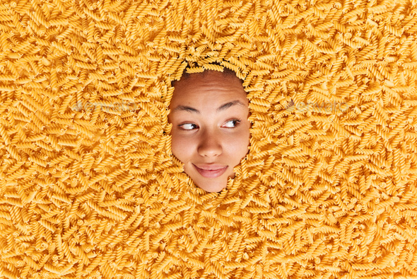 People and food concept. Pretty womans face stuck in pasta background ...
