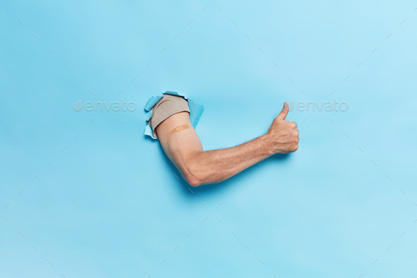 Horizontal shot of unrecognizable human breaks arm through paper blue ...
