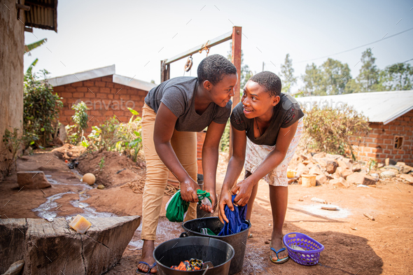 Two african girls wash clothes by hand using soap and a bucket ...