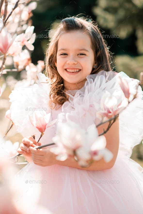 Happy cheerful child girl posing with magnolia flowers in garden ...