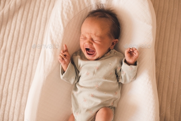 Upset and sad infant child crying and scream in bed with colic pain or ...