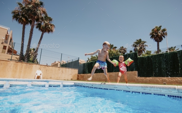 Two kids run and jump to the swimming pool at the sunny summer day ...