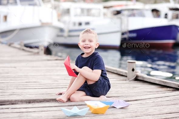 Smiling kid boy 5 year old playing with paper boats over sea background ...