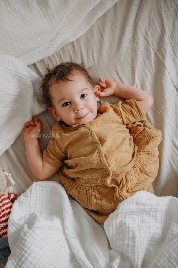 Infant girl portrait overhead in bed after sleeping time in neutral ...