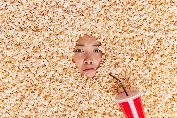 Upset stressed Asian woman shows only face buried in popcorn drinks ...