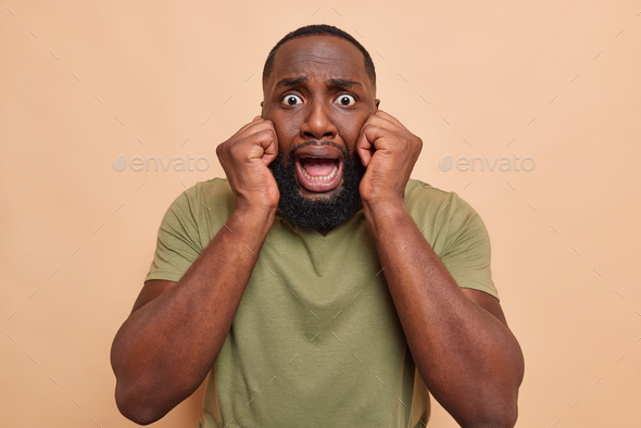 Scared worried dark skinned man keeps hands on face stands alarmed ...