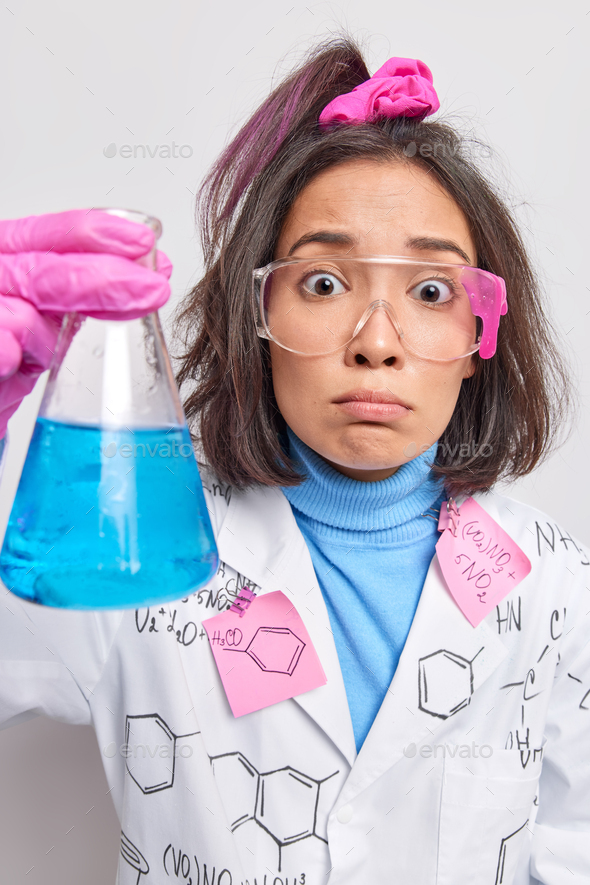 Displeased inexperienced Asian female researcher holds glass beaker ...