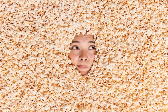 Overhead shot of young female face pocking through popcorn background ...