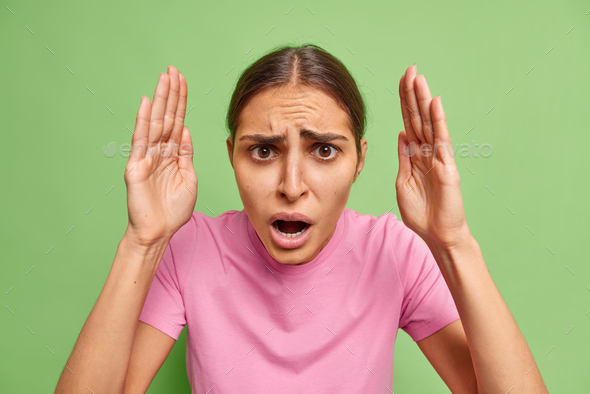 Indoor shot of frustrated young woman raises palms looks unhappily has ...