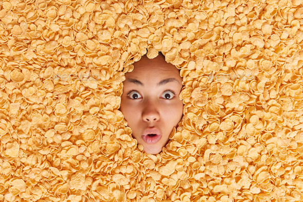 Ethnic woman sticks face through yellow cornflakes has surprised ...