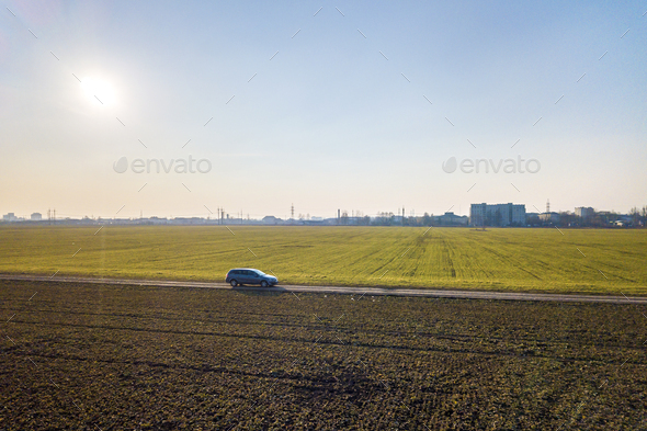 Aerial view of car driving by straight ground road through green fields ...