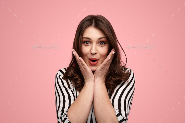 Surprised young lady shouting and touching cheeks against pink ...