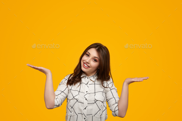 Positive young lady shrugging shoulders against yellow background Stock ...