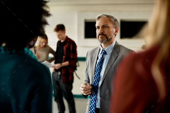 University professor communicating with his students in a hallway ...