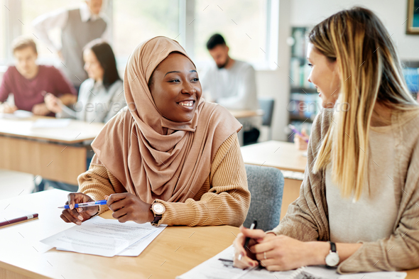Happy black Muslim student talking to her classmate at college ...