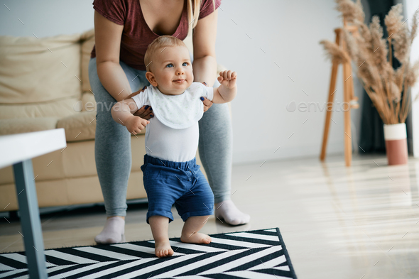 Cute baby boy walking with help of his mother at home. Stock Photo by ...