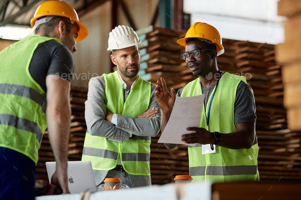 Warehouse workers analyzing paperwork with their manager at lumber ...