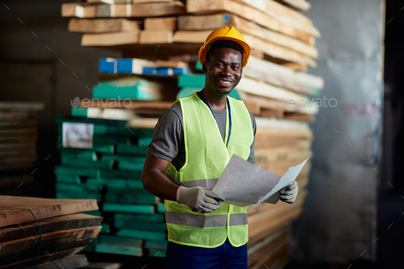 Happy black warehouse worker going through paperwork at wood ...