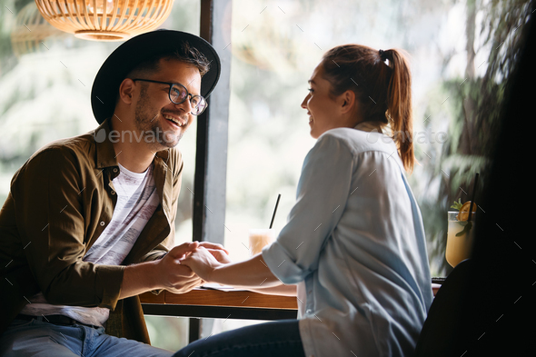 Young happy couple holding hands while talking to each other in cafe ...