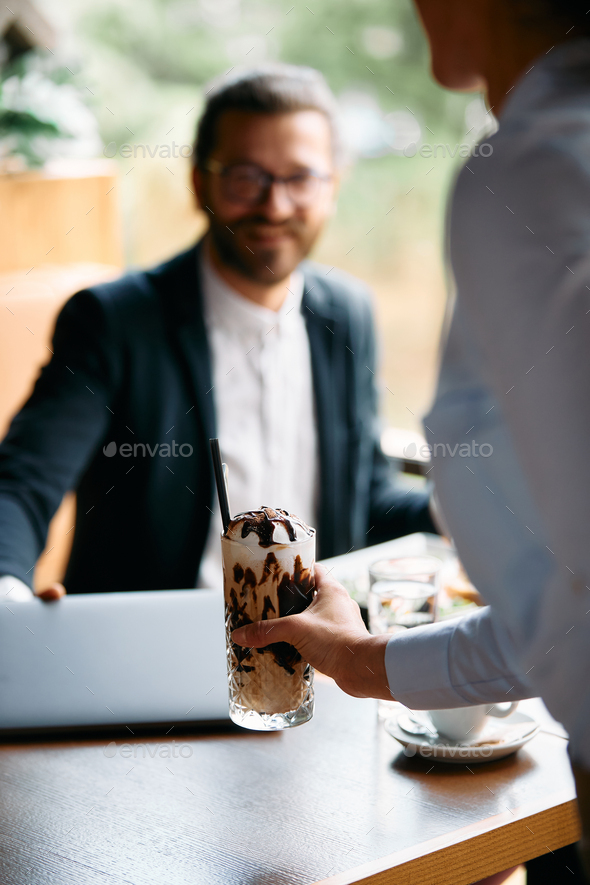 Close-up of waitress serving iced coffee to her customer in a cafe ...
