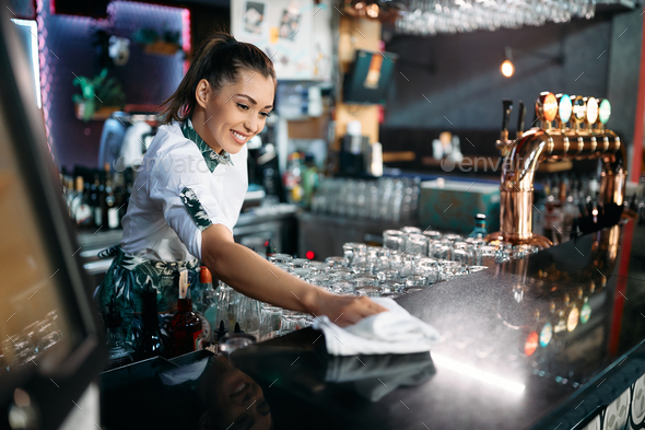 Happy female bartender wiping bar counter after working hours. Stock ...
