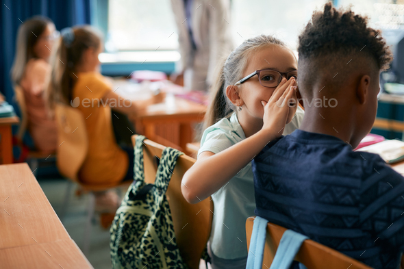 Schoolgirl whispering something into classmate's ear during class in ...