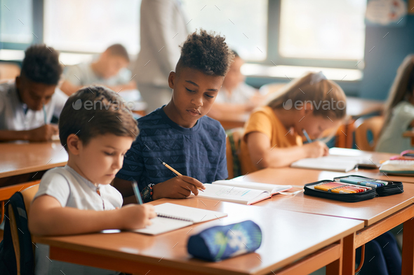 African American schoolboy and his classmates writing during class in ...