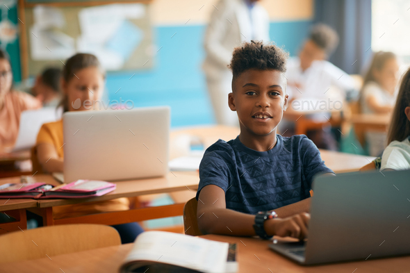 Smiling black elementary student using laptop while e-learning during ...