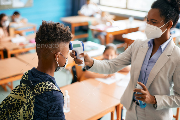 Elementary school teacher measuring temperature of schoolboy in ...