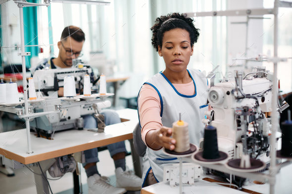Black seamstress adjusting thread on sewing machine while working at ...