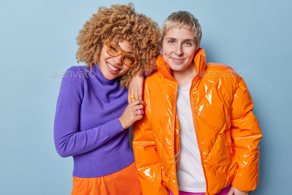 Happy attractive young women stand closely to each other wear bright ...
