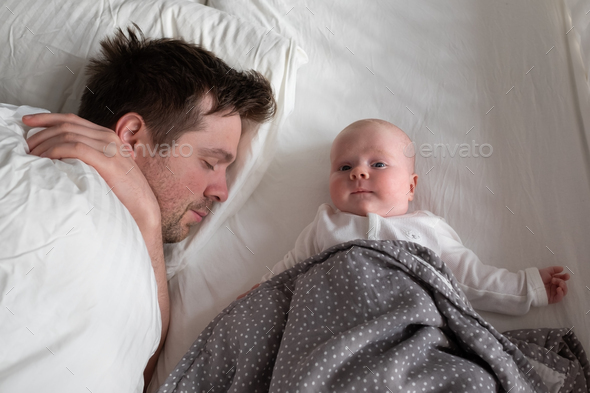 Sleeping father and cute child resting together in bed. Stock Photo by koldunova_anna