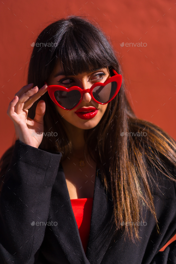 Brunette girl in a portrait on a red background with glasses hearts ...
